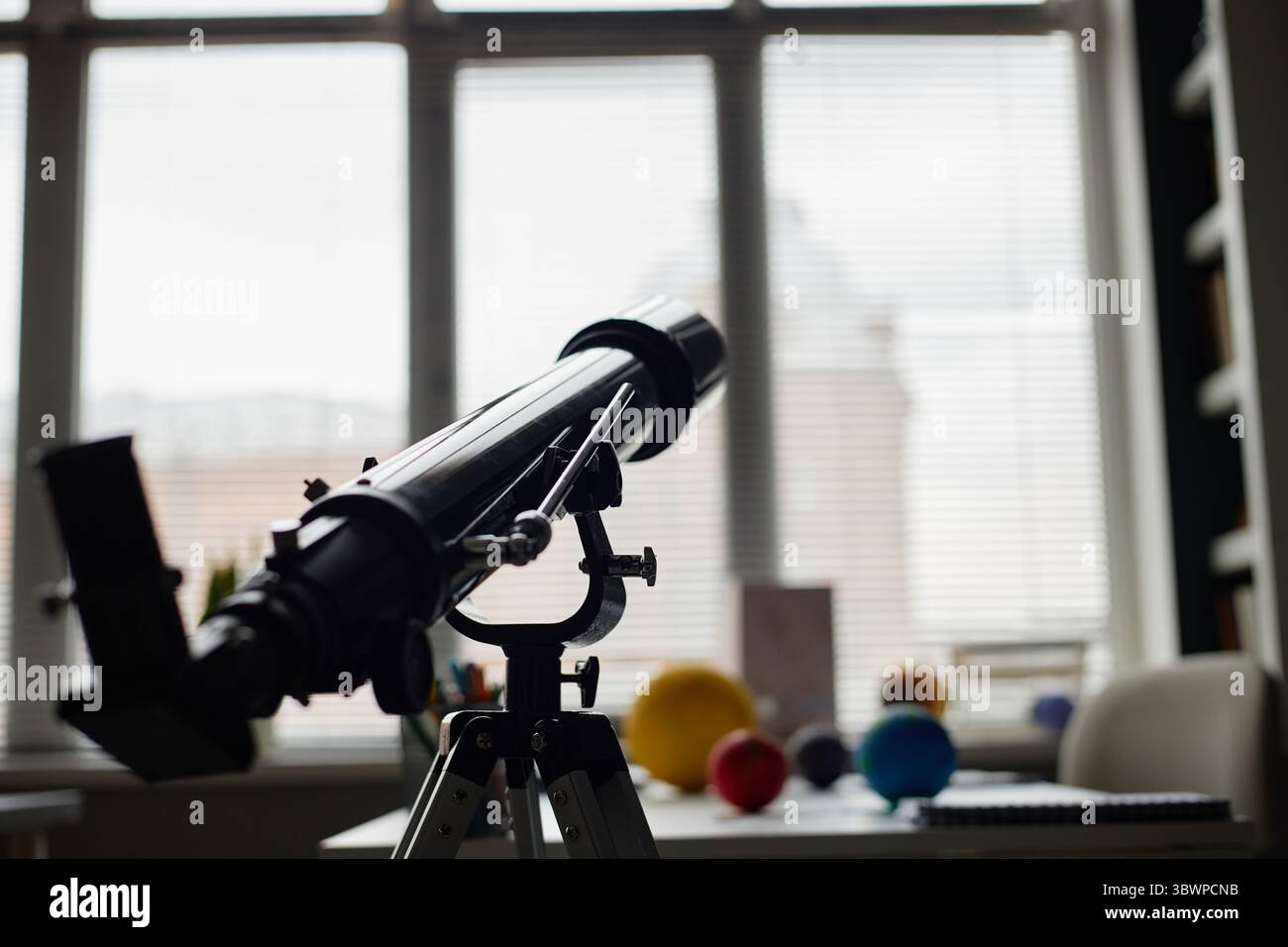 Telescope standing on tripod in front of large window with blurred ...