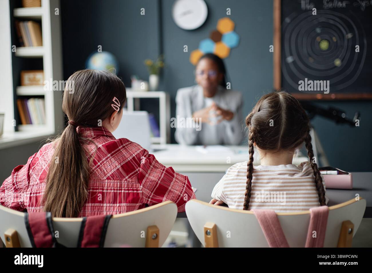 Two Caucasian girls sitting in classroom facing Black female teacher ...