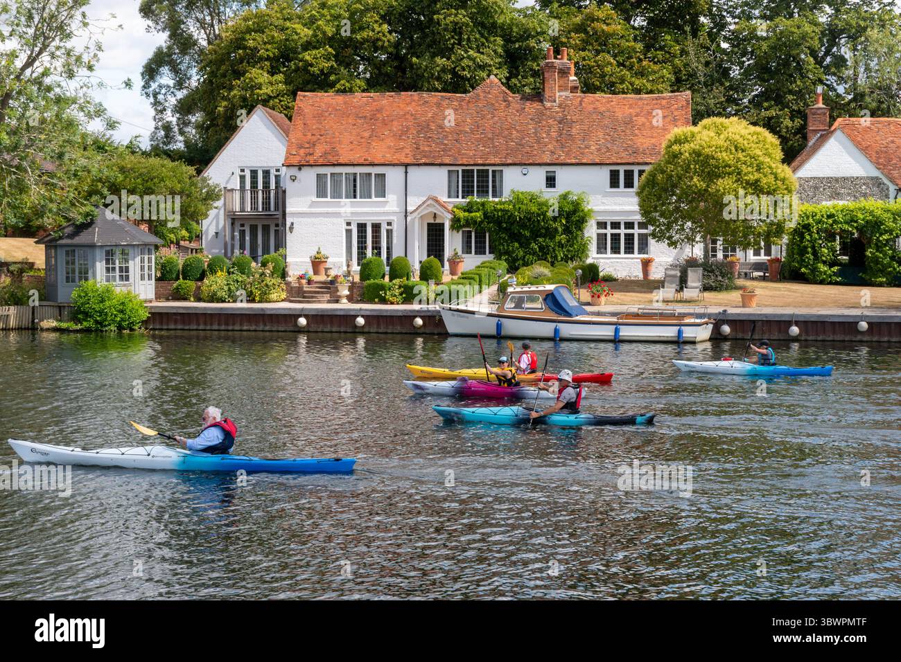 A group of kayakers paddling on the River Thames in front of riverside ...