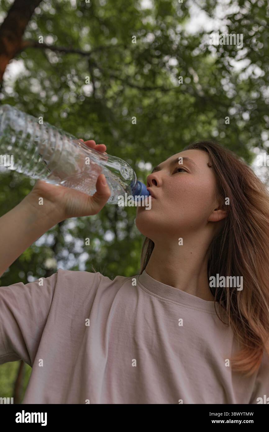 Young woman in light pink shirt drinking water from plastic bottle ...