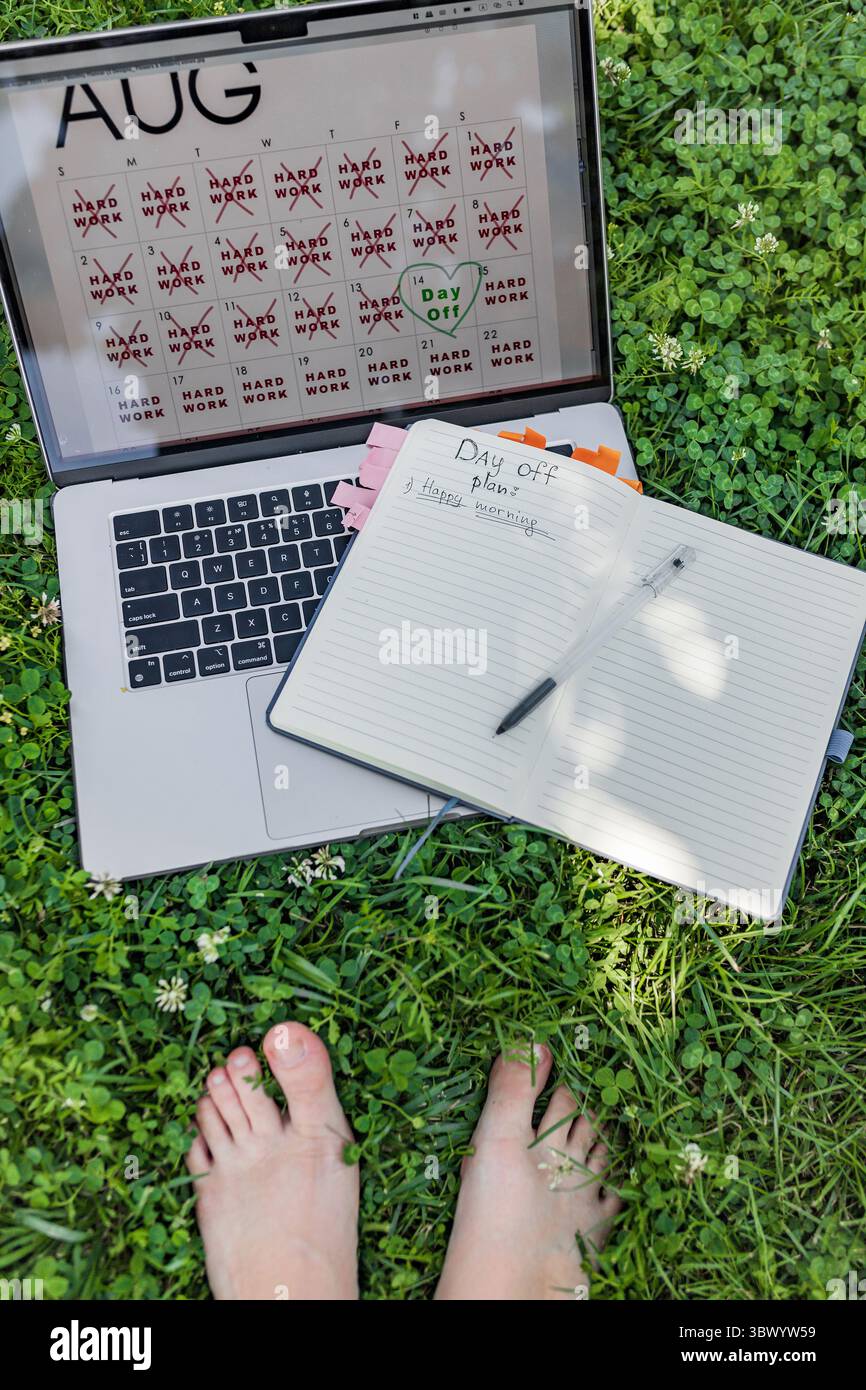 Feet resting on grass near laptop and notebook with handwritten day off ...