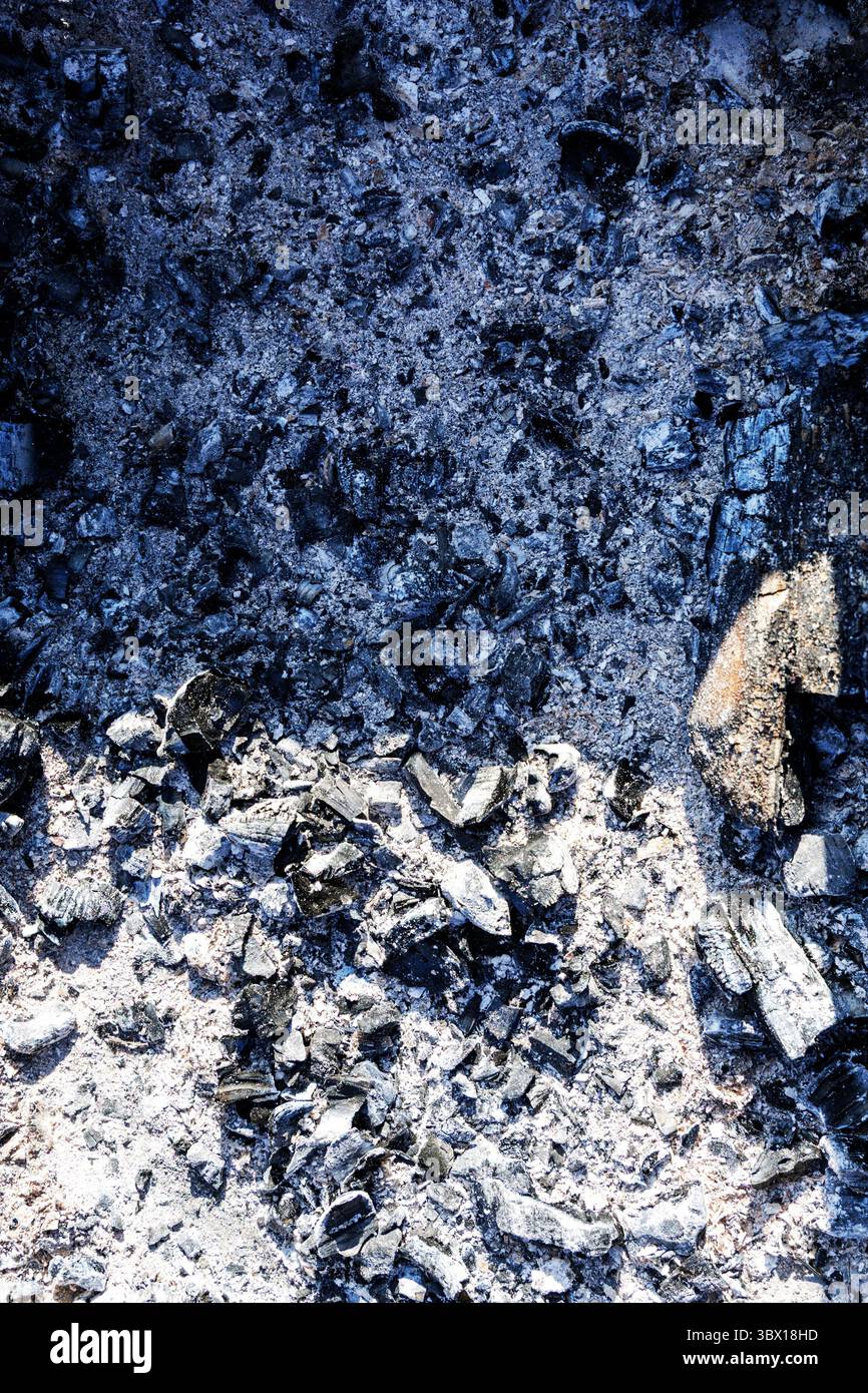 A textured close-up of dark ash and charred wood remnants from a fire ...