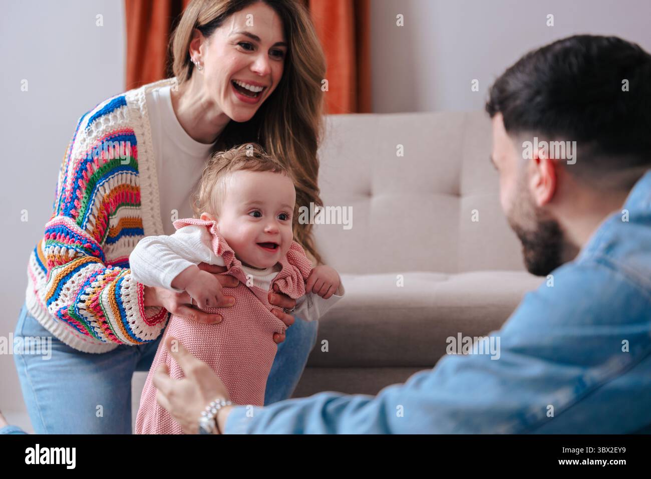 Parents helping baby girl take first steps on carpet at home with joy ...
