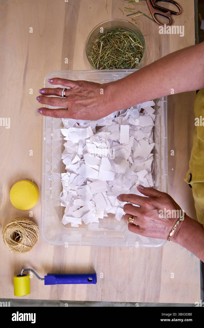 Woman placing torn white paper into water container for pulp making ...
