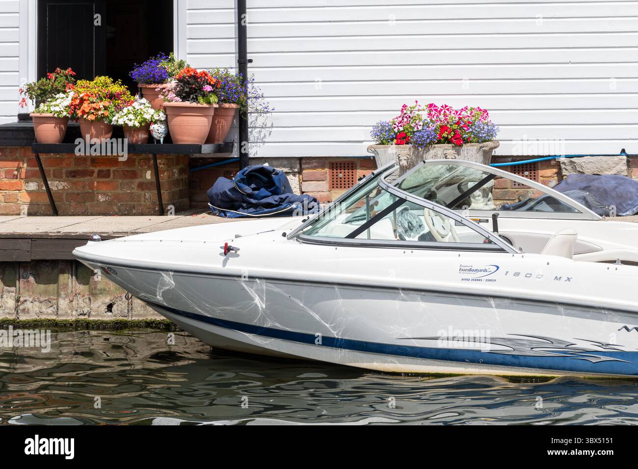 Display of colourful flowers in pots outside a boathouse with a motor ...