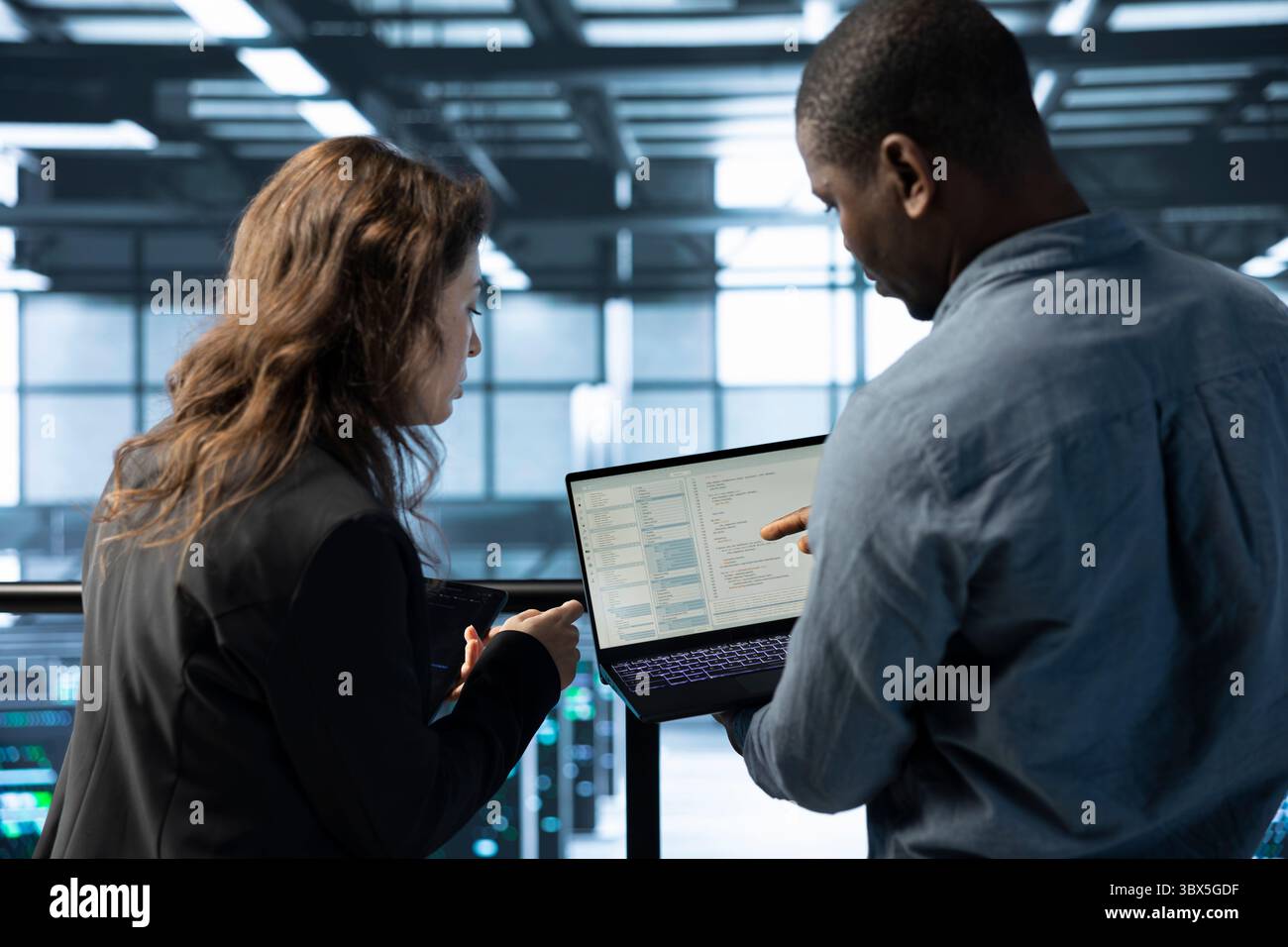 Programmers in data center workspace coding on laptop, analyzing ...