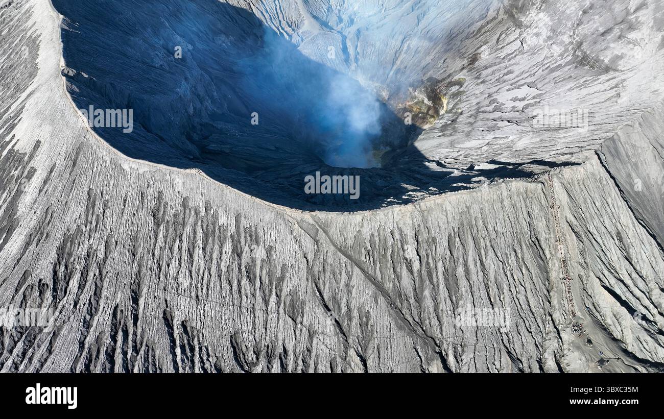 The steep crater rim reveals dramatic textures and deep shadows as blue ...