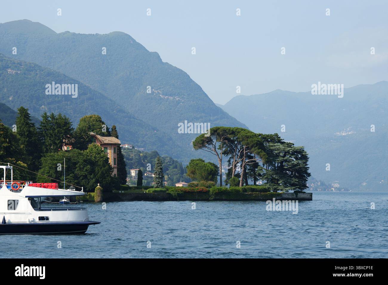 Lake Como with a boat and cypress trees in Italy among the Alps Stock ...