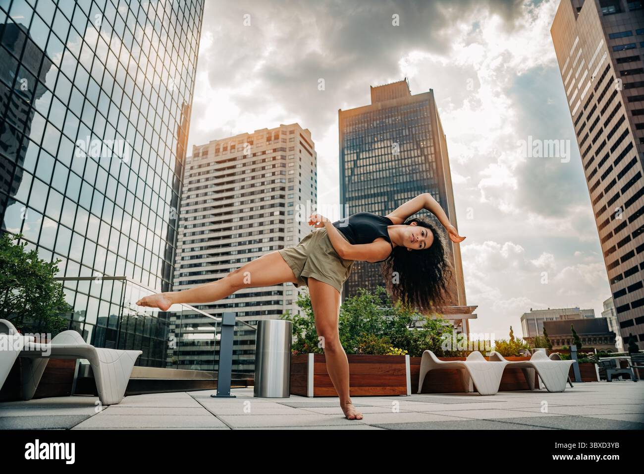 Woman poses in dance stretch on rooftop with dramatic skyline Stock ...