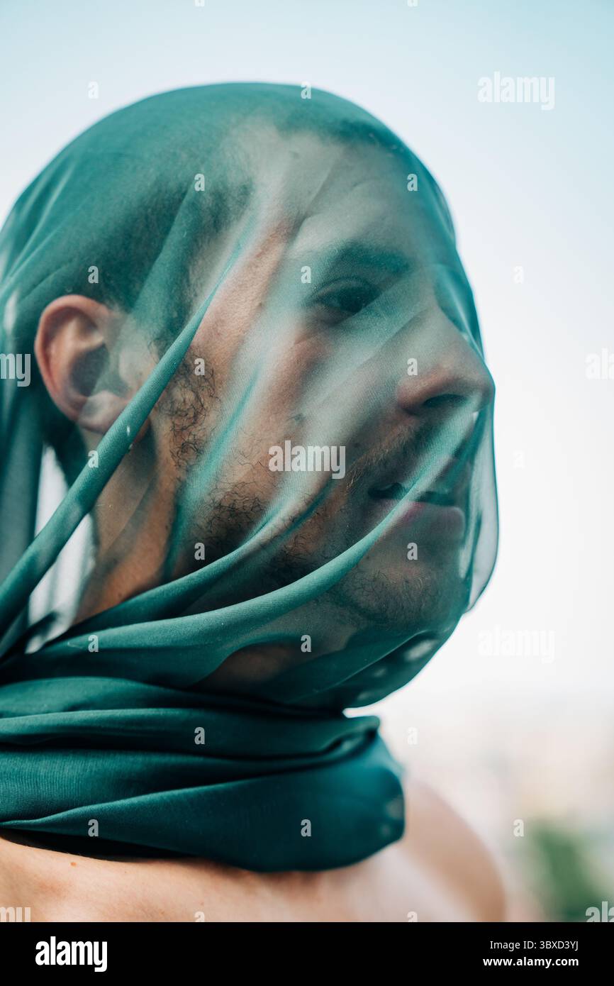 Close-up of man's face wrapped in flowing green translucent fabric ...