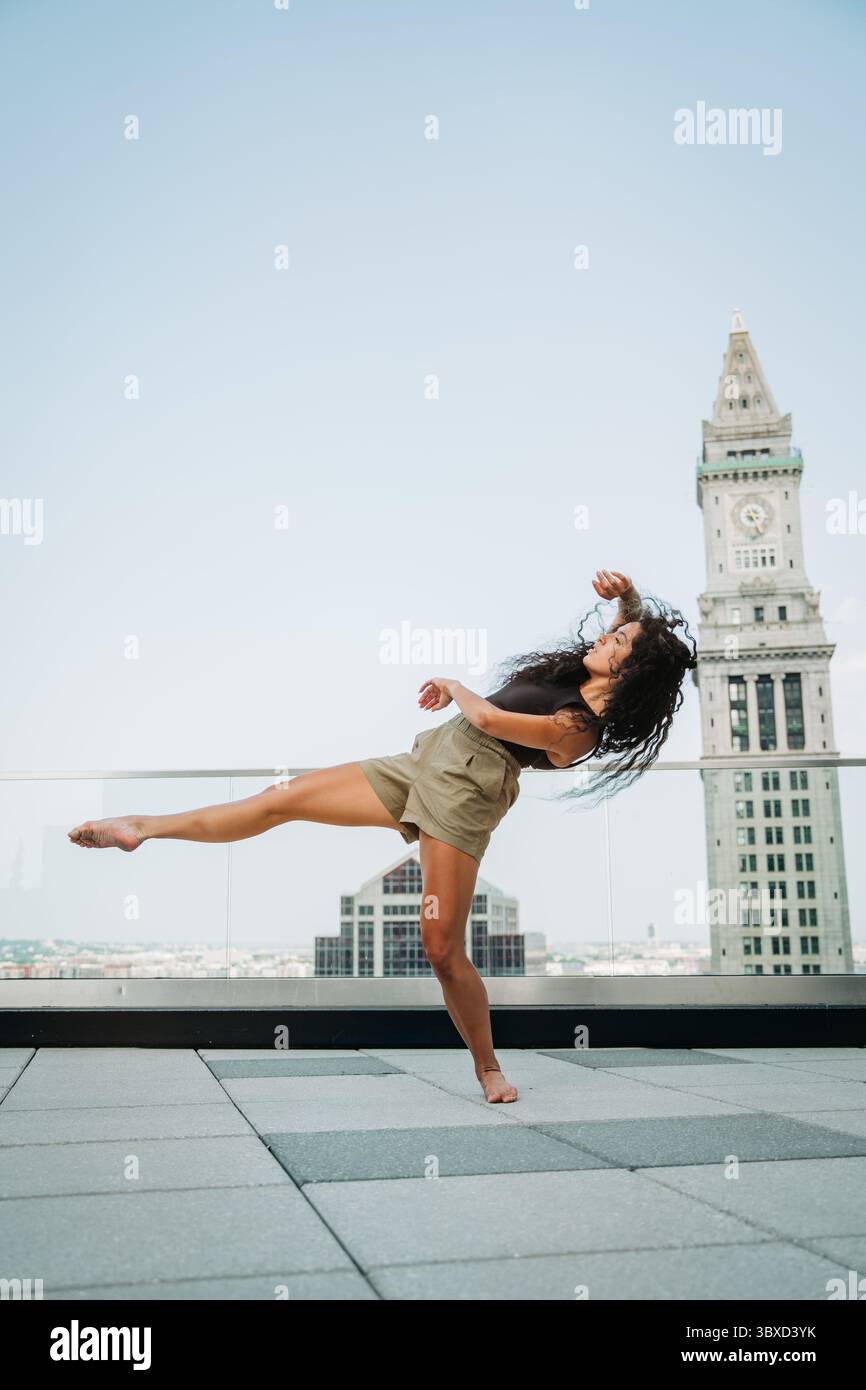 Woman dances barefoot on rooftop with Boston clock tower behind Stock ...