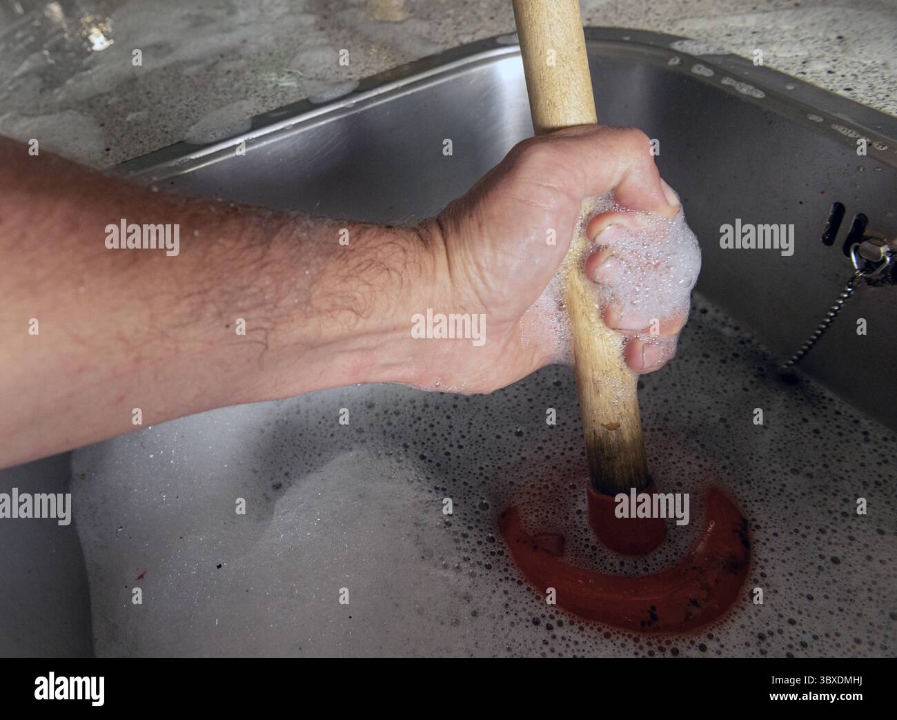 General stock - mans hand using a plunger to unblock a kitchen sink ...
