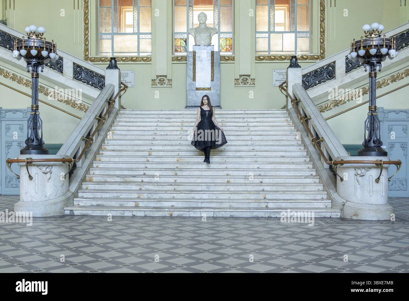 Beautiful girl in black dress running down wide stairs in hall ...