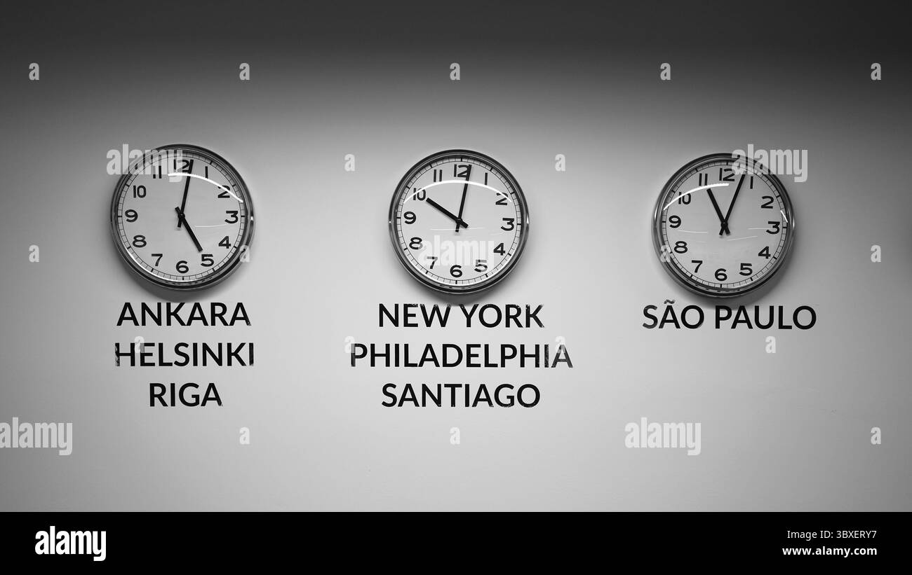 Many wall clocks on the white wall of business office showing time of ...
