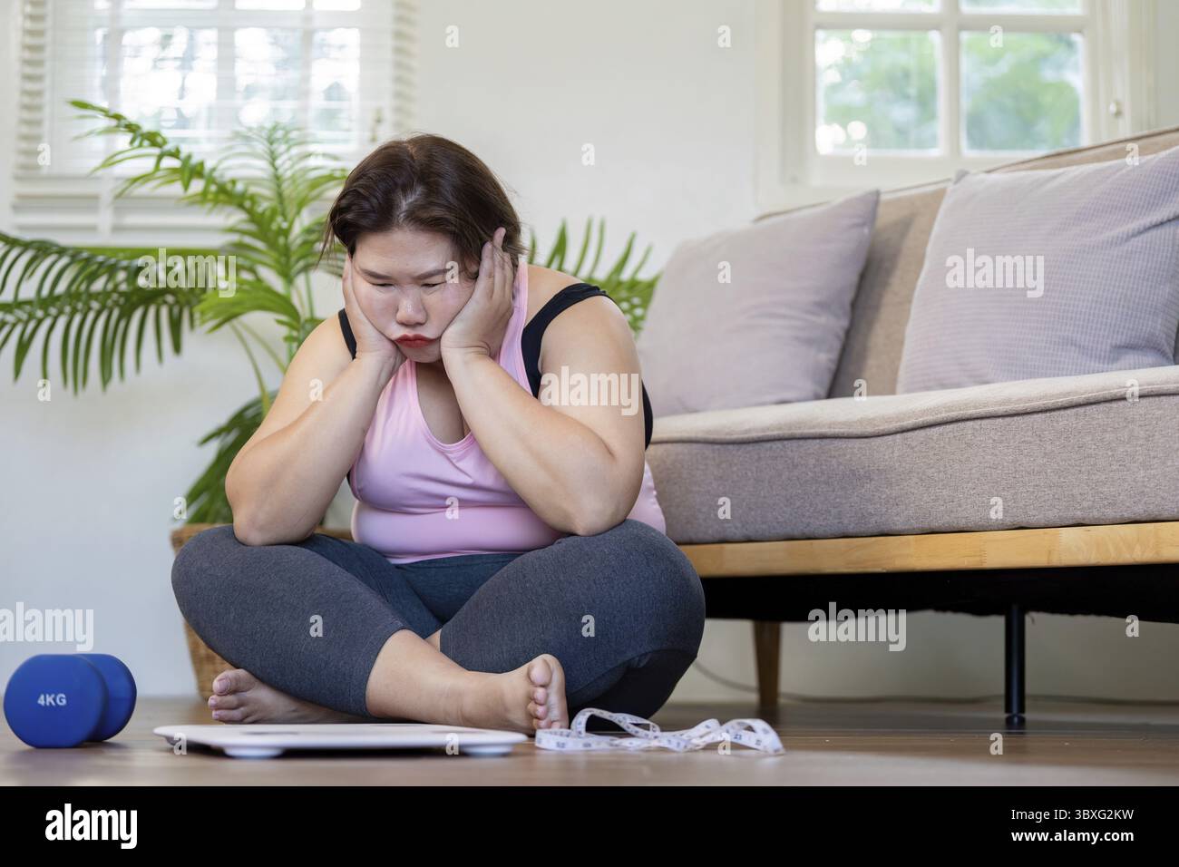 An overweight woman sits on the floor with her hands on her face ...