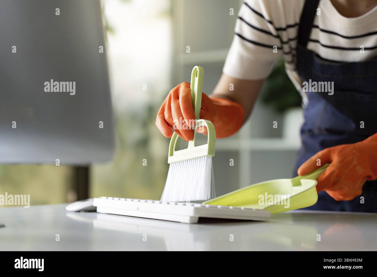 An individual using a brush and pan to clean a keyboard on a desk ...