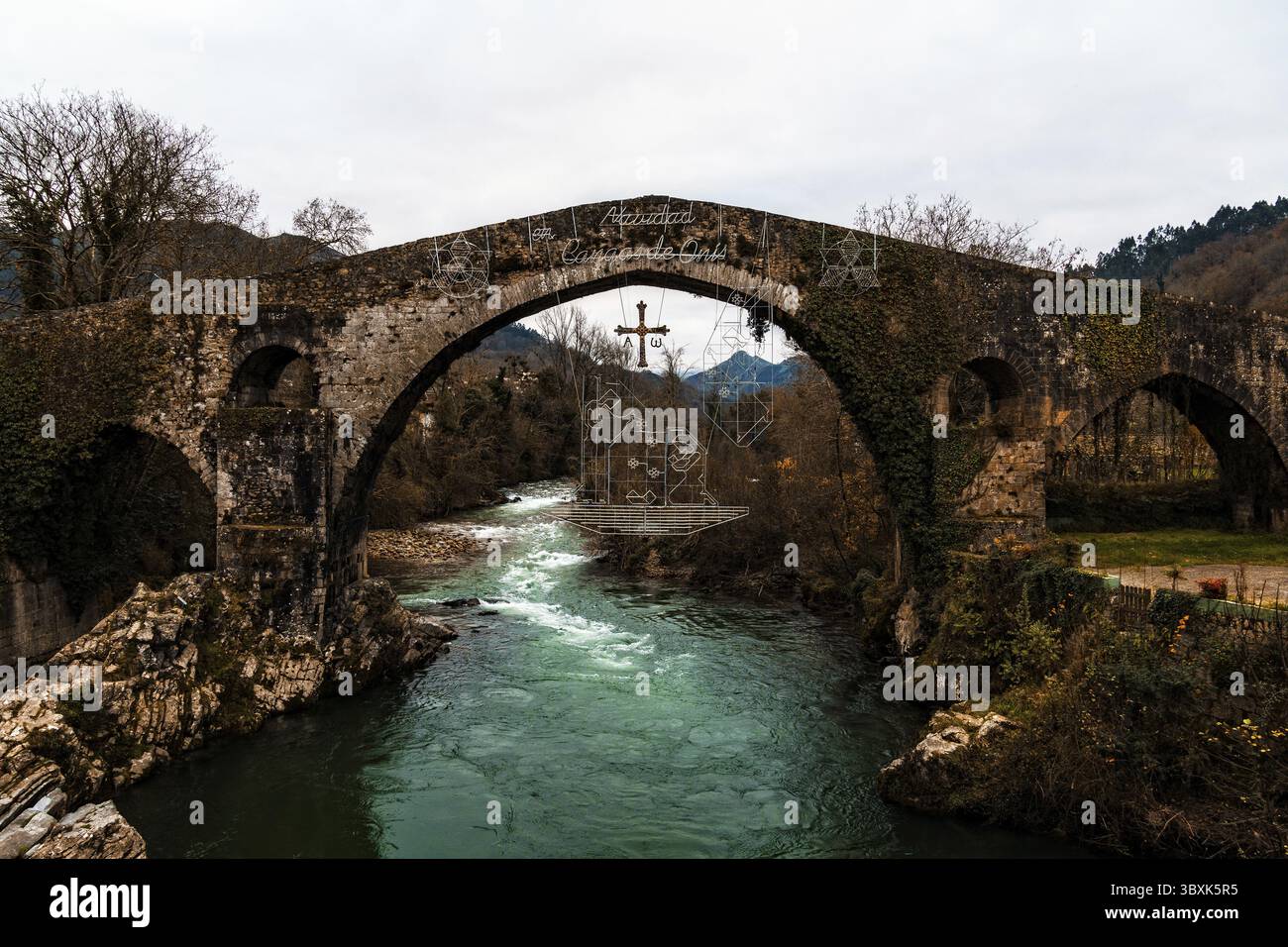 Ancient stone bridge arching over a flowing river, with a cross visible ...