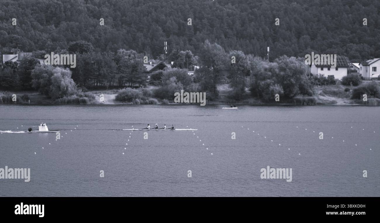 Rowing team practices on calm river waters guided by a boat. Scenic ...