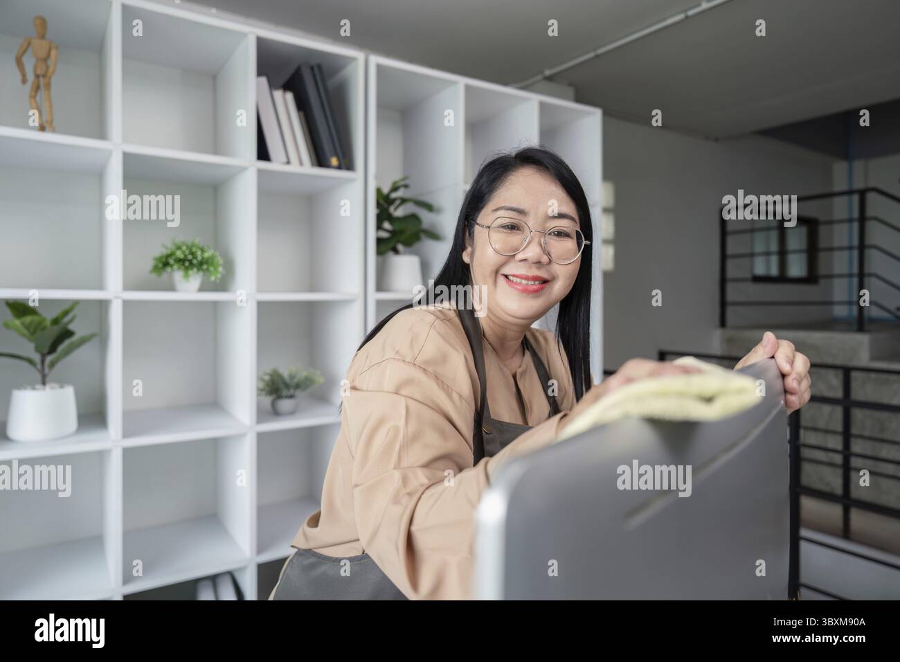 A cheerful housekeeper in a modern home, cleaning with a cloth ...