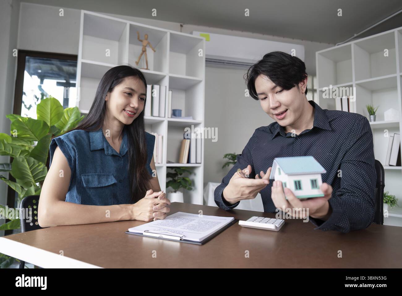 Real estate agent presenting a house model to a client in a modern ...