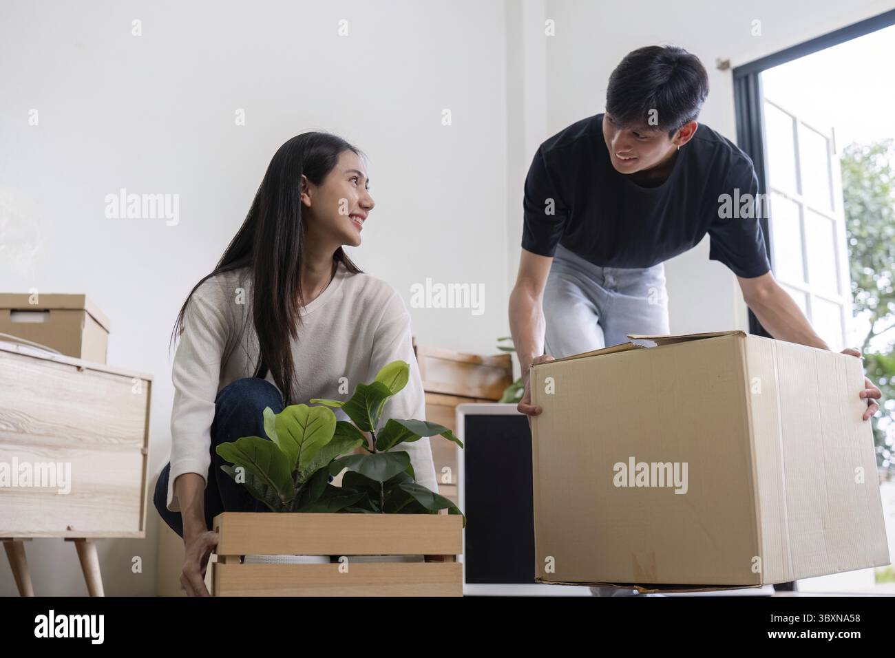 A cheerful couple moving into their new house, carrying boxes and ...