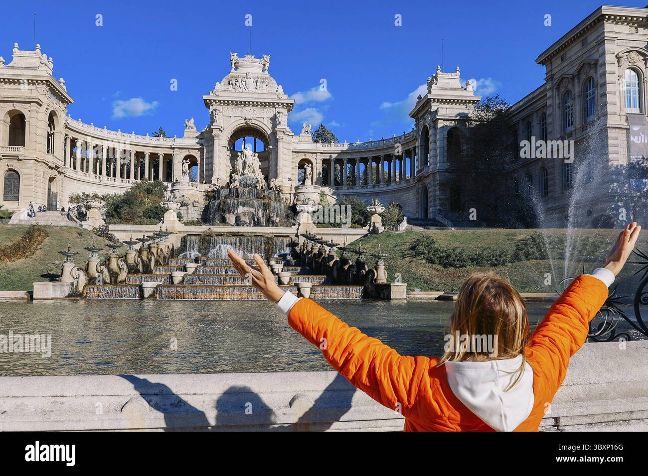 Woman in orange with her arms raised admires power of palace. View of ...