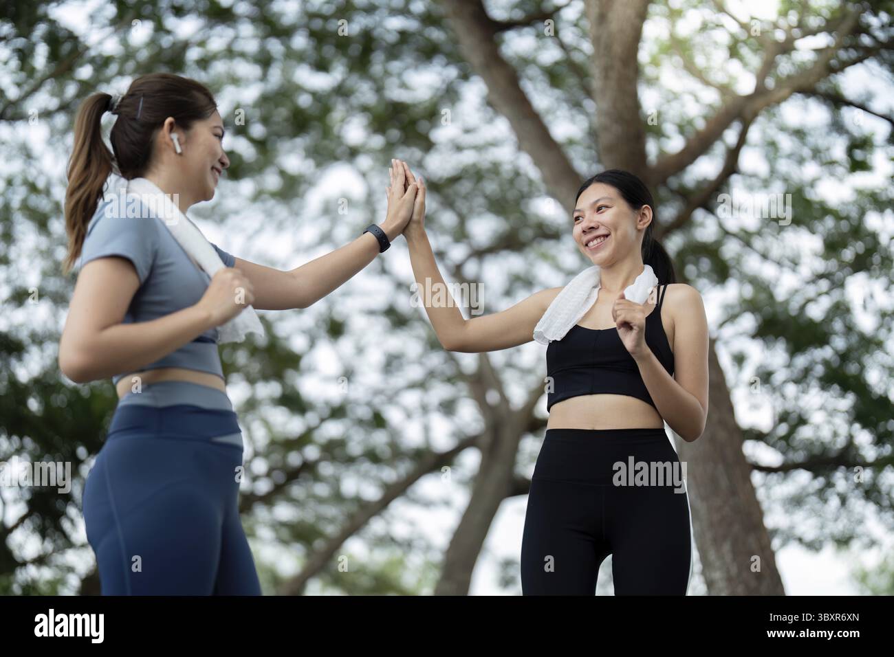 Two women high fiving and smiling after a morning run in the park ...