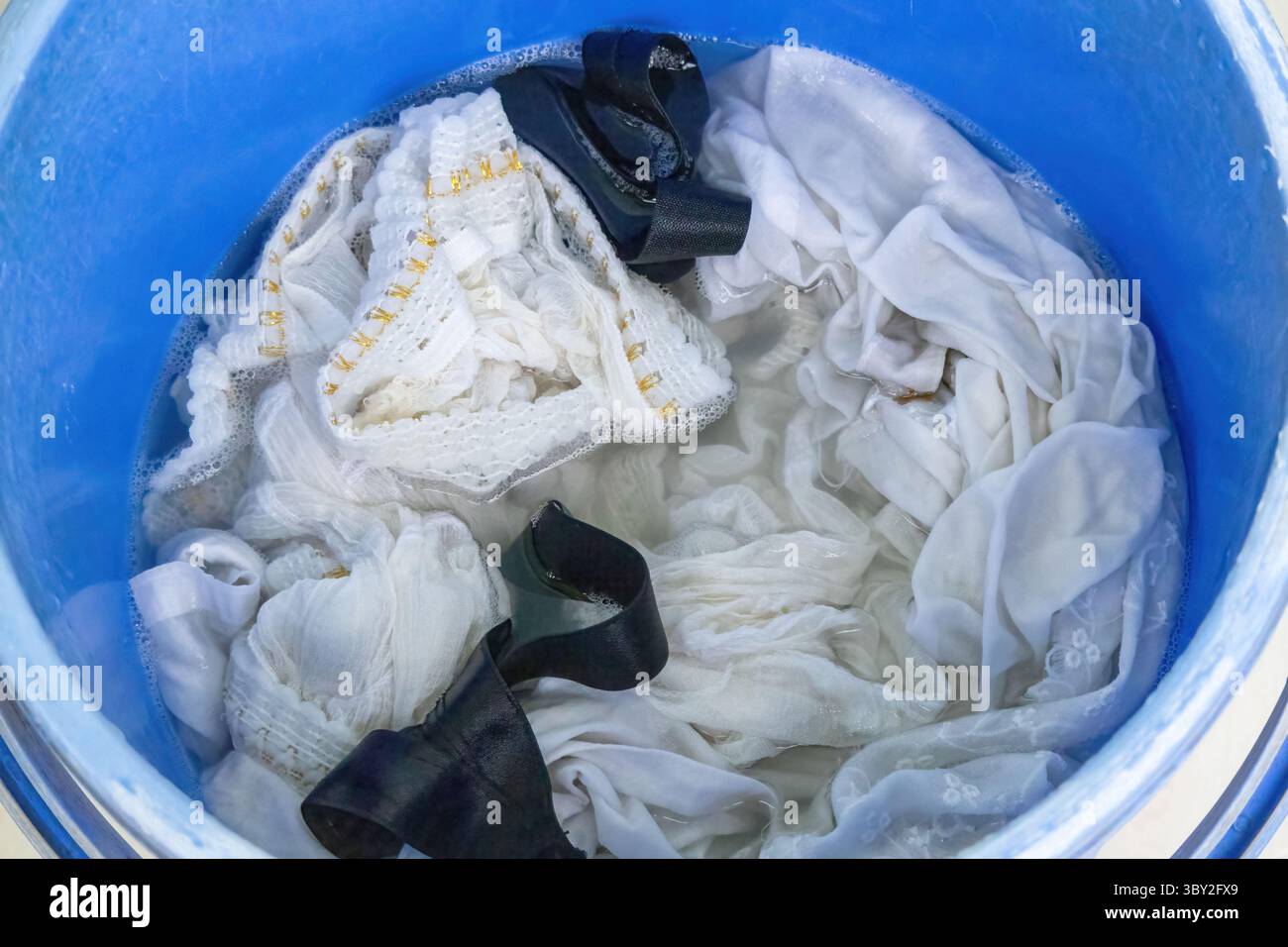 Detailed view of laundry in a blue plastic bucket, clothes fully ...