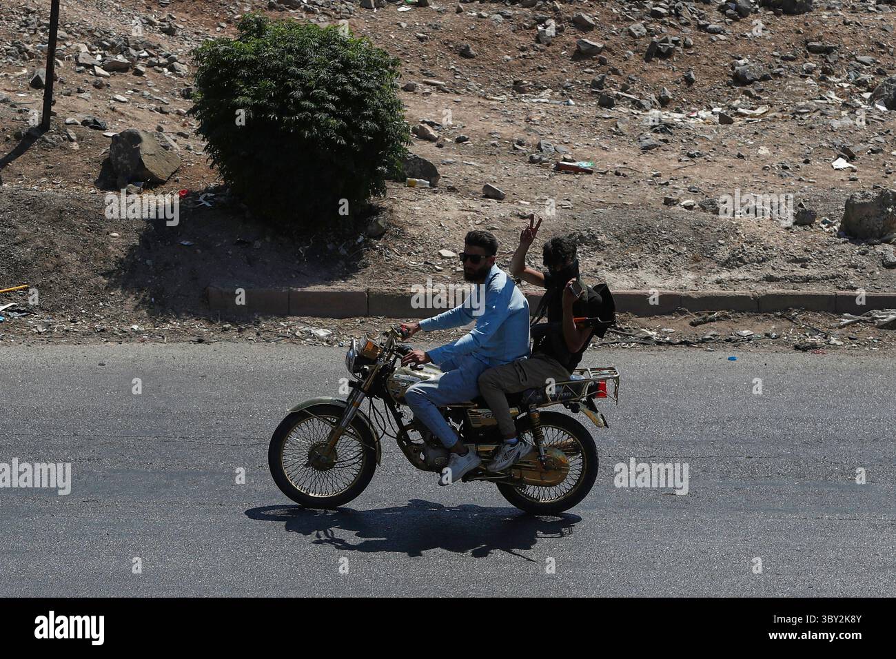 A fighter flashes a victory sign while carrying a rifle as he rides on ...