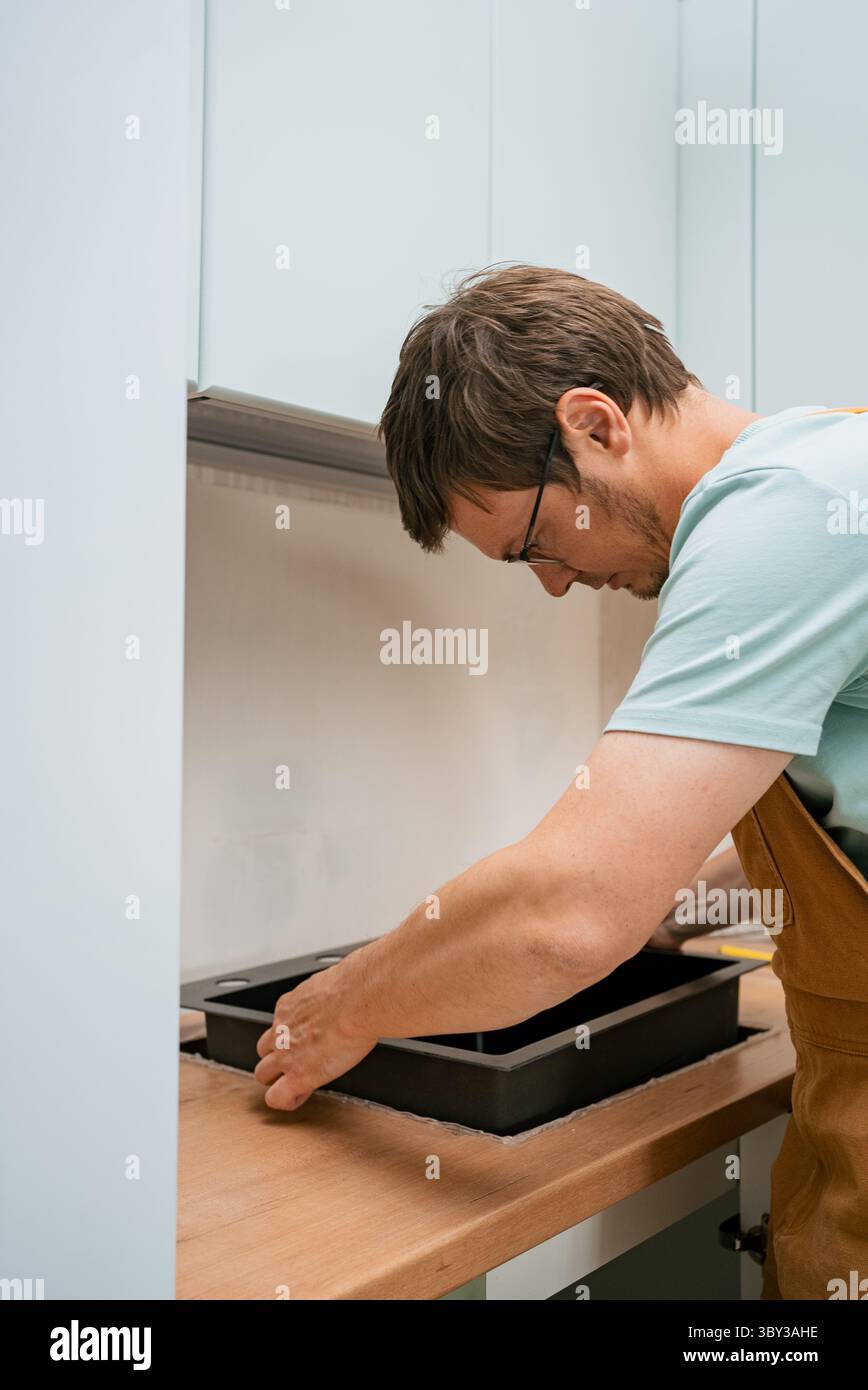 Professional plumber carefully installing a new kitchen sink into a ...