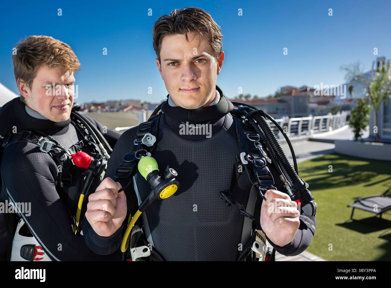 Two scuba divers wearing wetsuits and full gear are helping each other ...