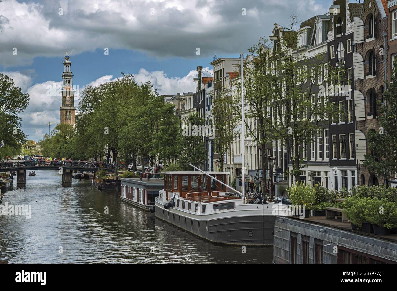 Tree-lined canal with old brick buildings, steeple, moored boats and ...