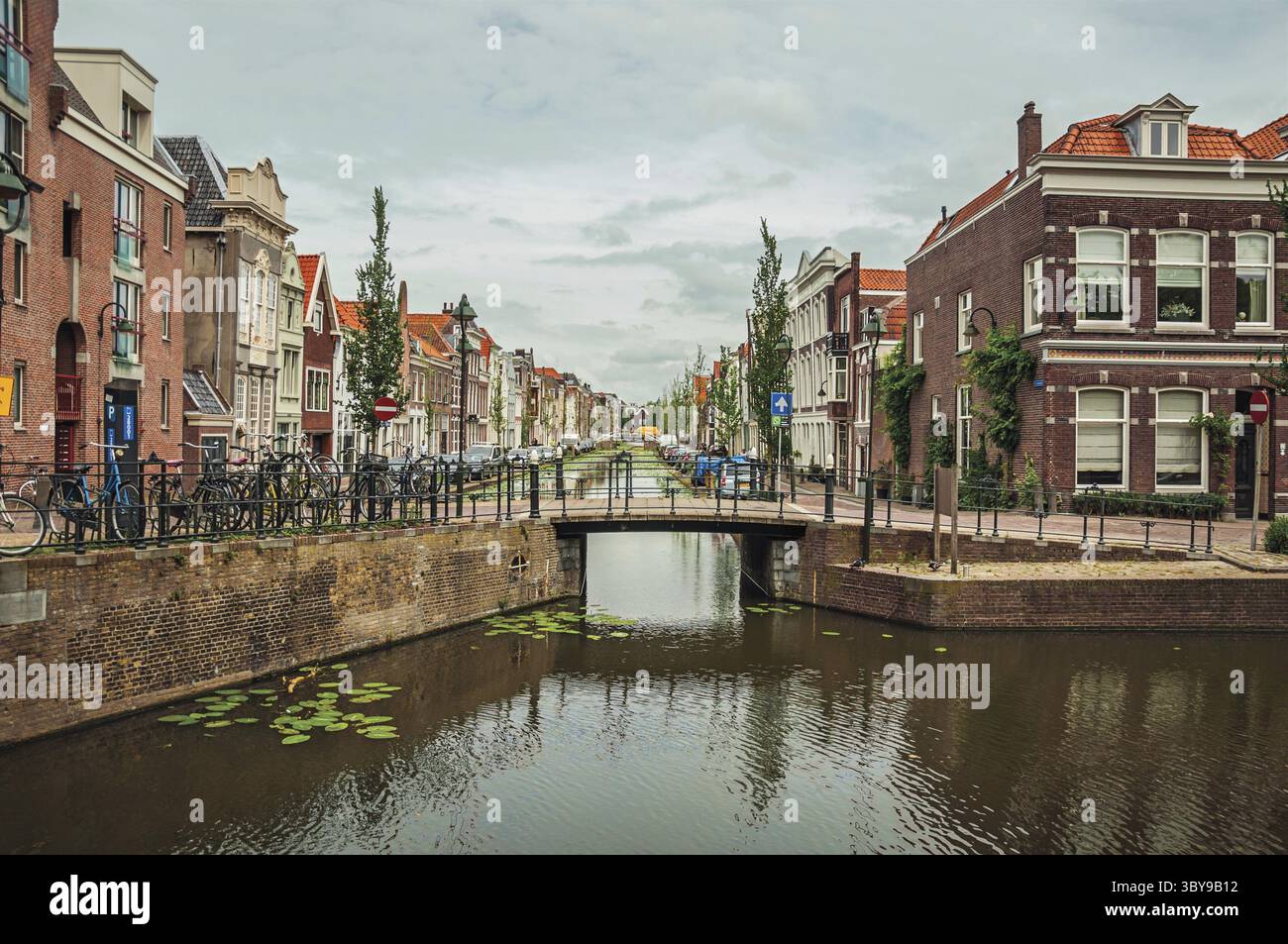 Tree-lined long canal with small bridge, brick houses on its bank and ...