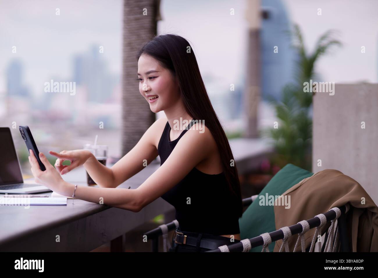 Confident Asian female manages digital tasks remotely from urban cafe ...