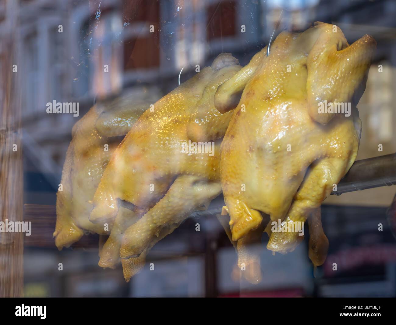 Three roasted chickens hanging in a window display, reflecting urban ...