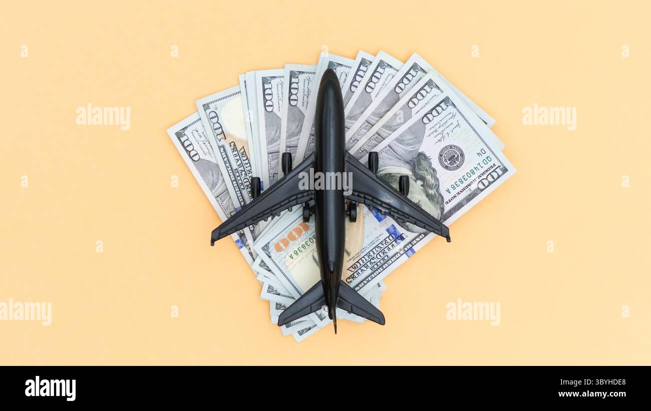 Black airplane model is positioned atop a pile of hundred-dollar bills ...
