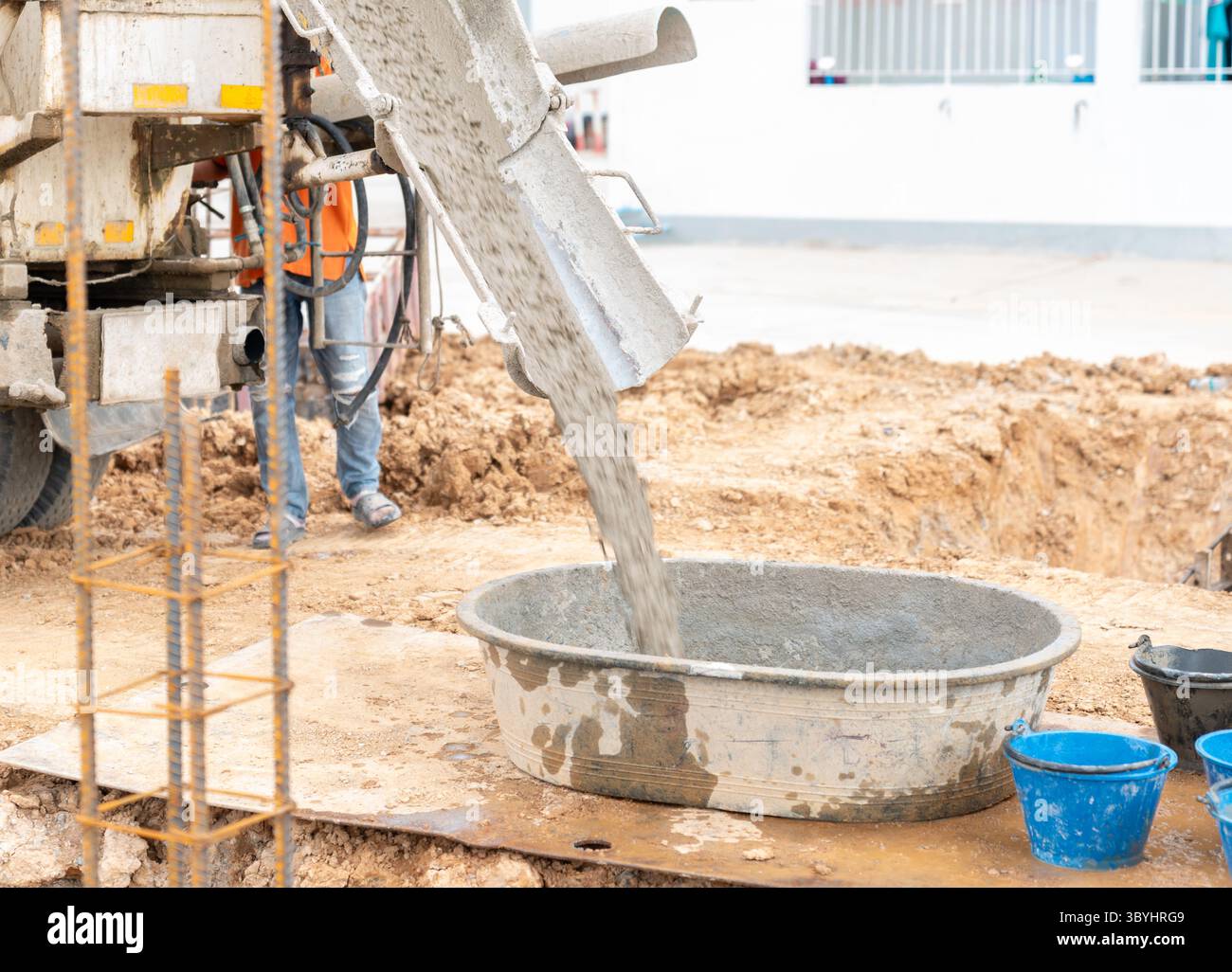 Concrete is being poured from a cement mixer truck chute into a large ...