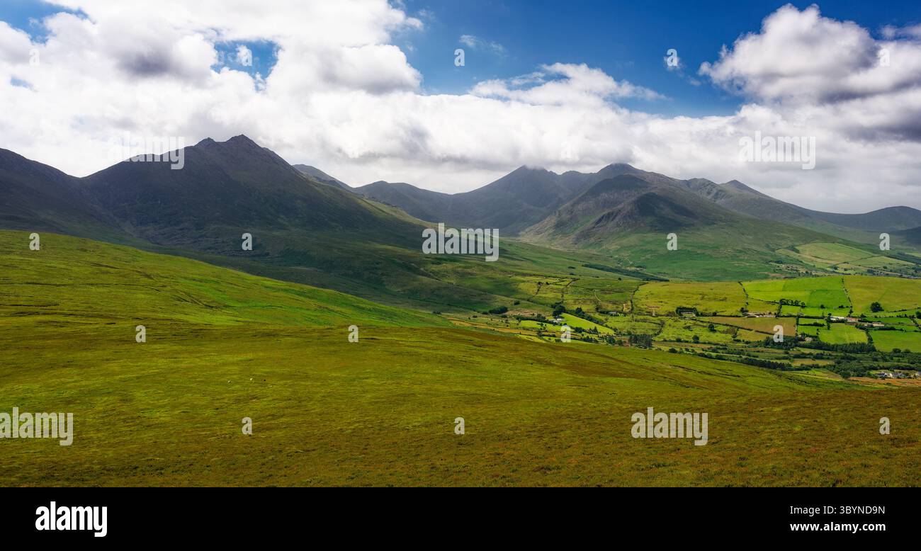 Gentle slopes of vibrant green lead the eye to towering peaks, a ...