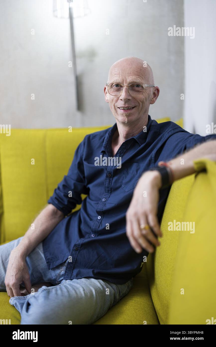 Portrait, older, bald man with glasses and blue shirt sits relaxed on a ...