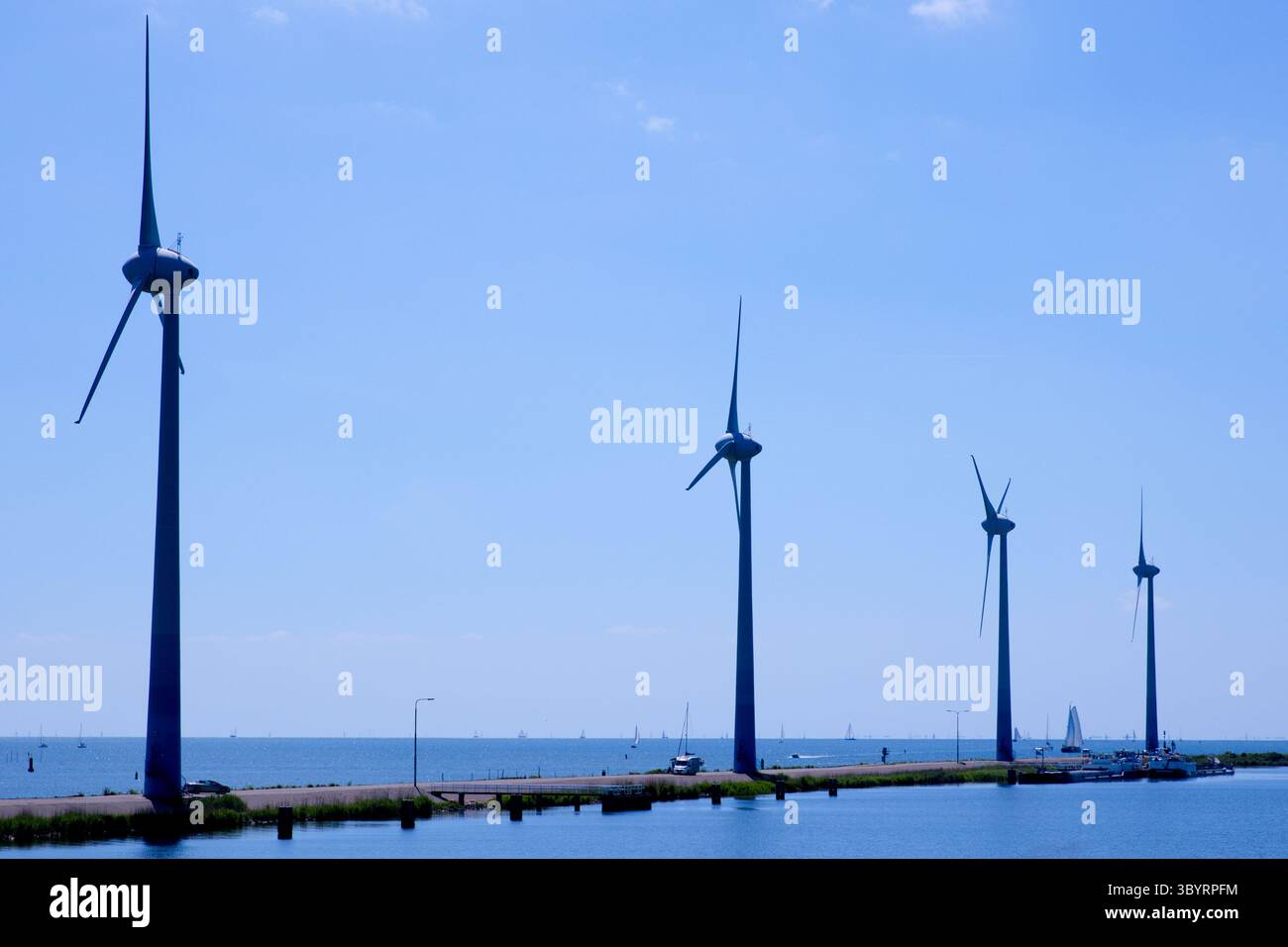 Four wind turbines stand on a narrow Amsterdam jetty over calm water ...