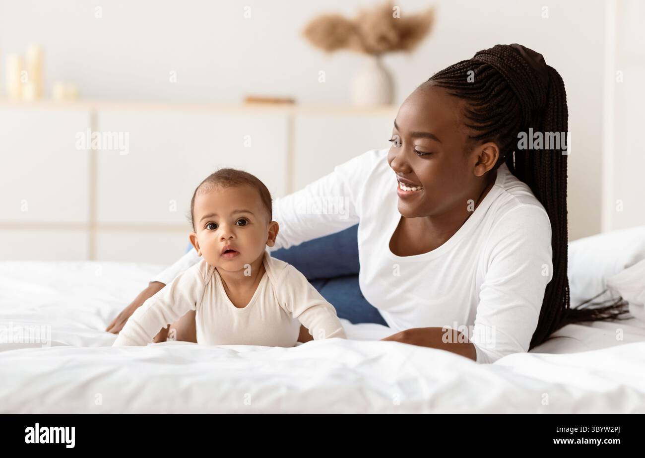 Cute little African American baby crawling in bed with mom Stock Photo ...
