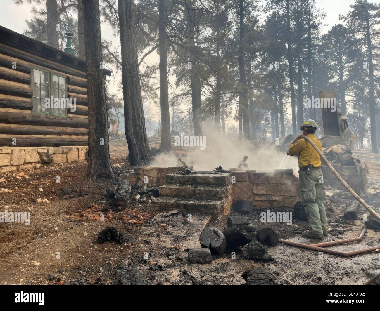 North Rim, United States. 13 July, 2025. A firefighter hoses down the ...