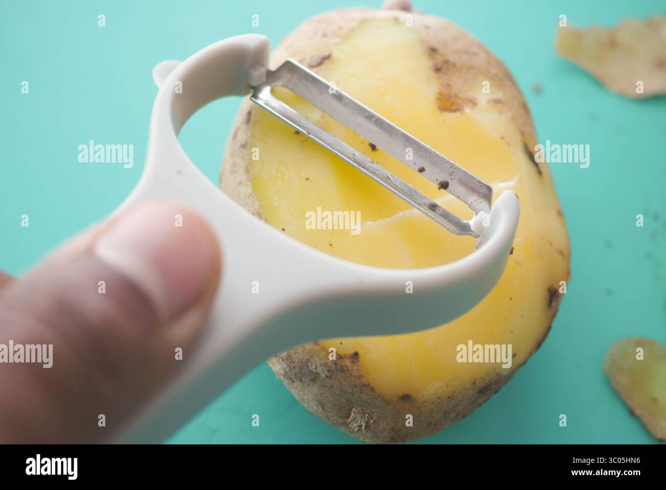 Peeling a potato with a vegetable peeler on a blue surface Stock Photo ...