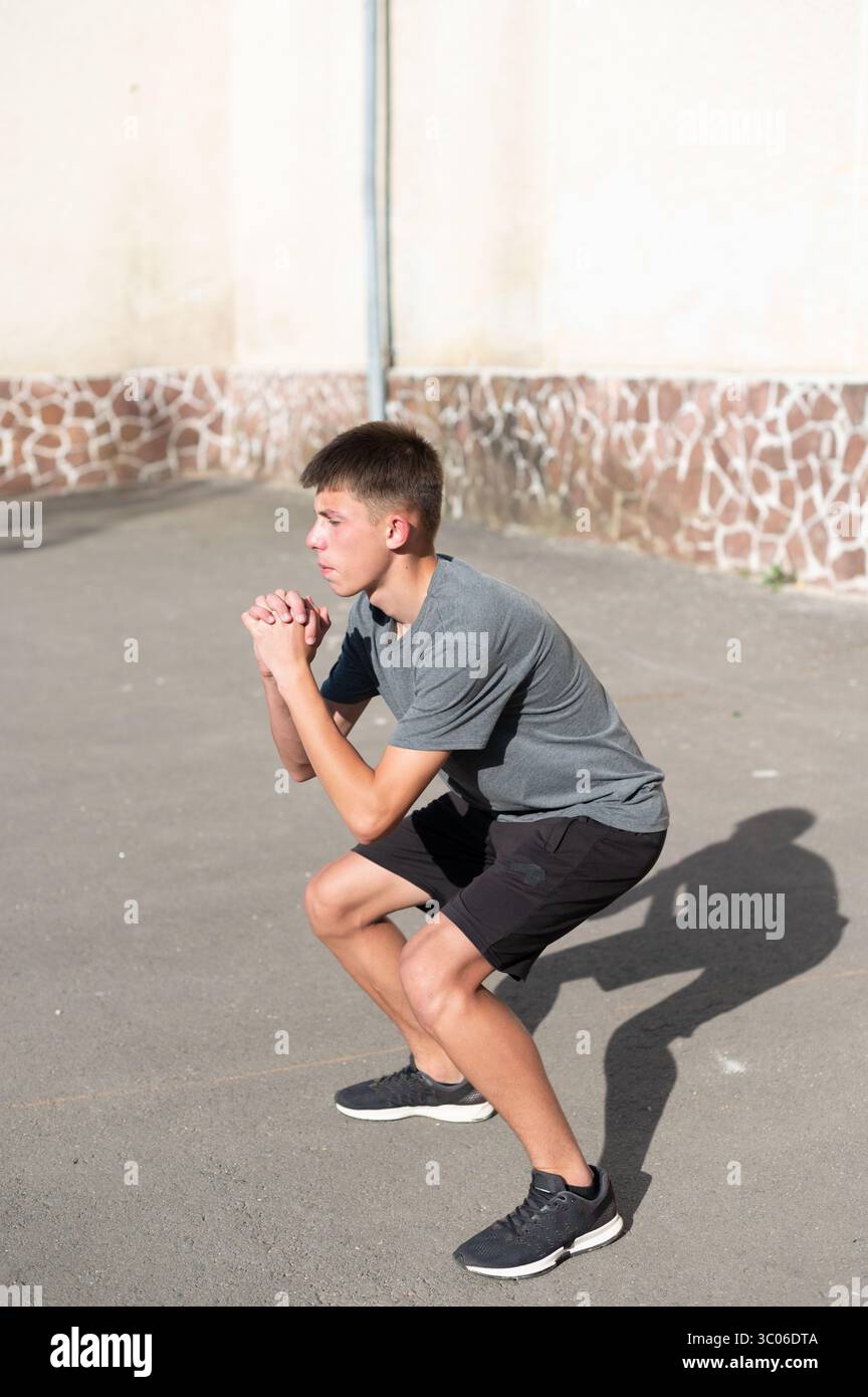 A young man performs squats as part of his outdoor fitness routine. He ...
