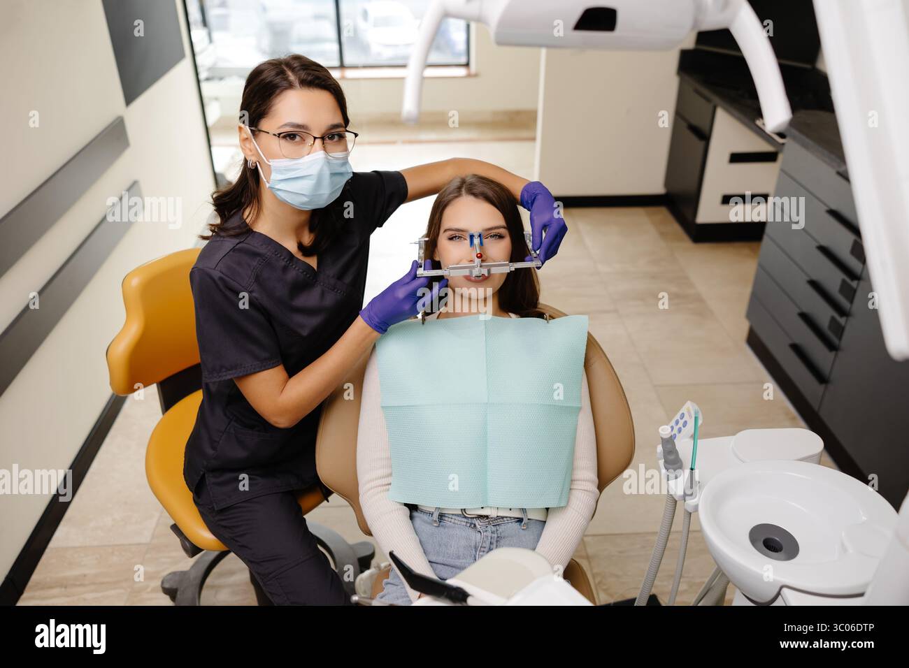 Female dentist trying on a facial arch for a patient sitting in a ...