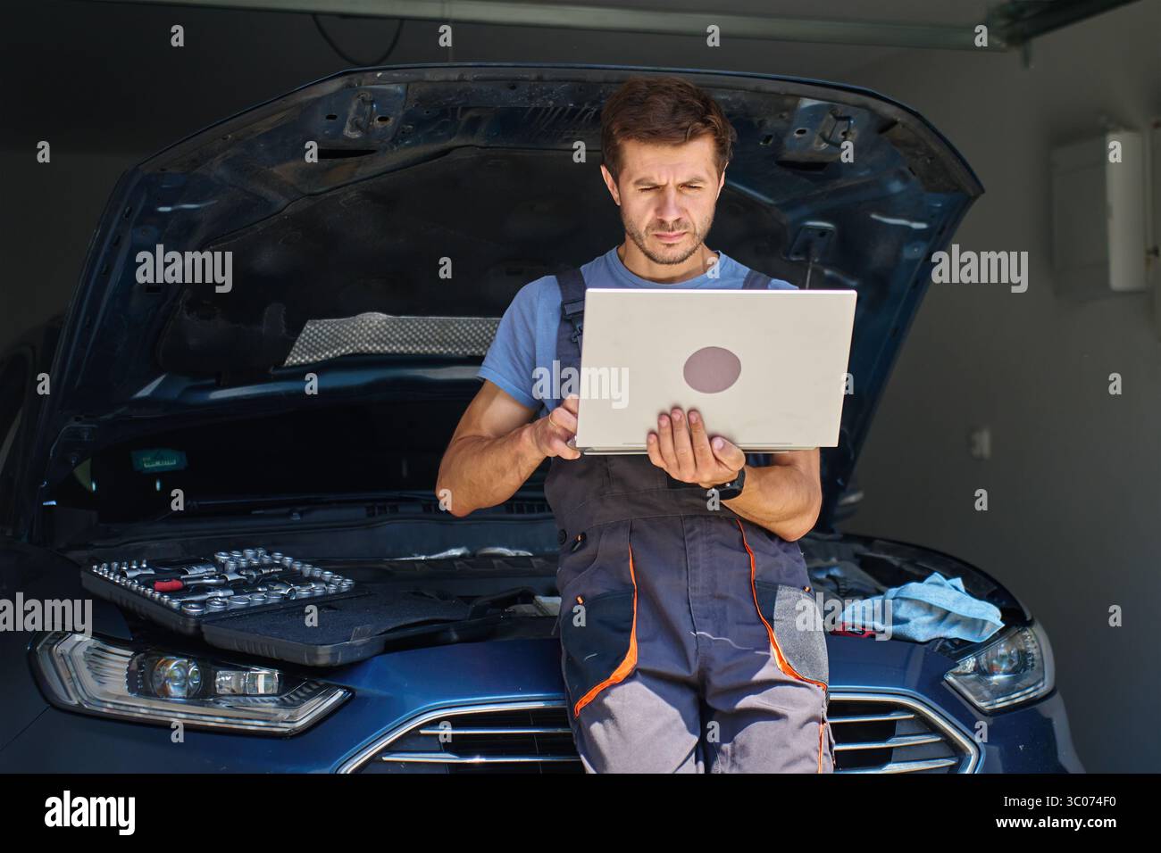 Auto mechanic stands near car with open hood, using laptop for ...