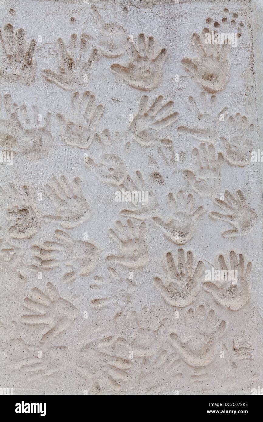 A textured wall features an array of handprints, creating a tactile and ...