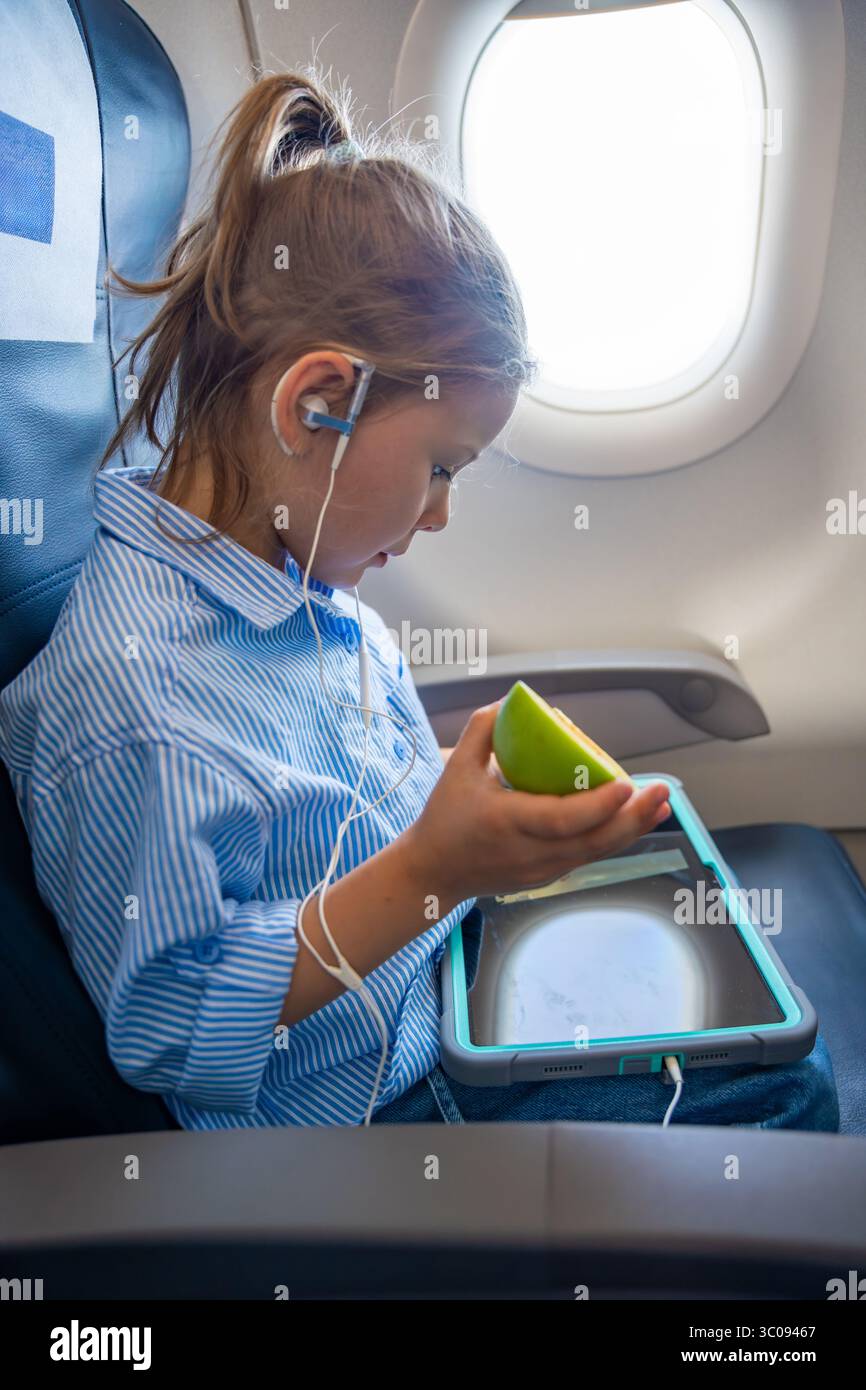 Little girl watching cartoons on tablet and eating green apple during ...