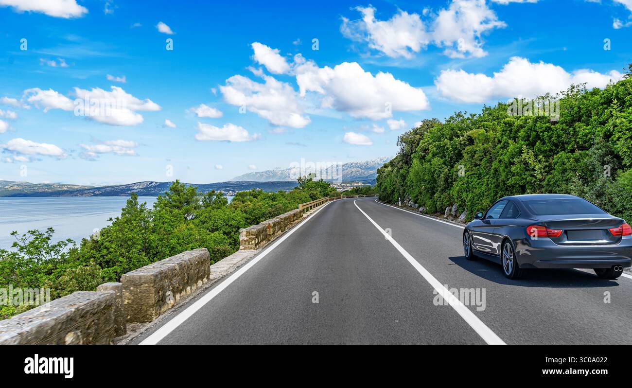 A car drives along a scenic coastal road with a bright blue sky and ...