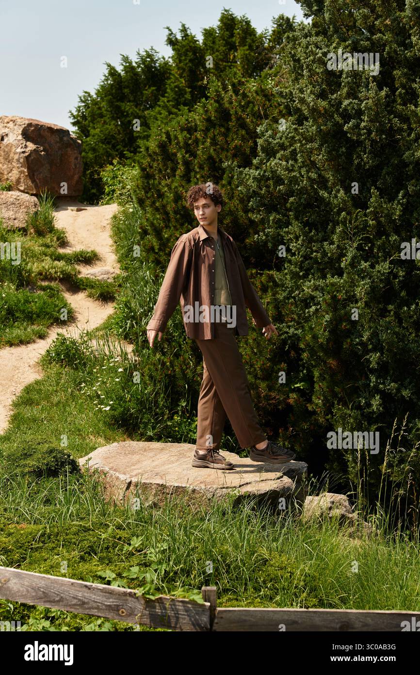 Curly-haired man in fashionable summer attire walks along a park's ...